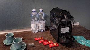 Uma mesa com duas garrafas de água, duas chávenas, uma máquina de café e vários pacotes de biscotti.