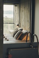 Cama com travesseiros e abajur, janela com vista para o exterior e parede de madeira.