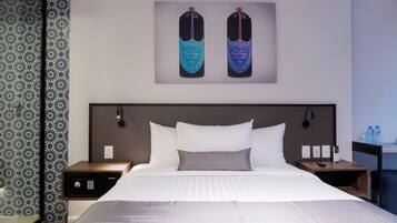 Quarto de hotel com uma cama grande, duas mesas de cabeceira, um criado-mudo, uma luminária na parede e um quadro emoldurado sobre a cama.