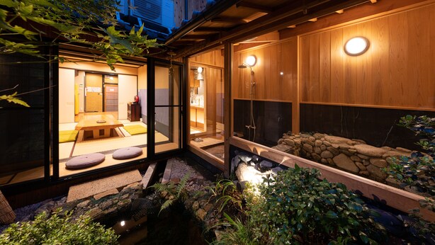 Um quarto tradicional japonês com piso de tatame, mesa de madeira baixa e um elemento decorativo de água em pedra.