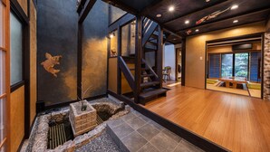 Um interior japonês tradicional com piso de tatame, decoração de carpas koi, um poço de pedra e uma escada de madeira.