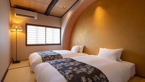 Quarto de hotel com duas camas, uma janela grande, uma luminária de chão e um ventilador de teto.