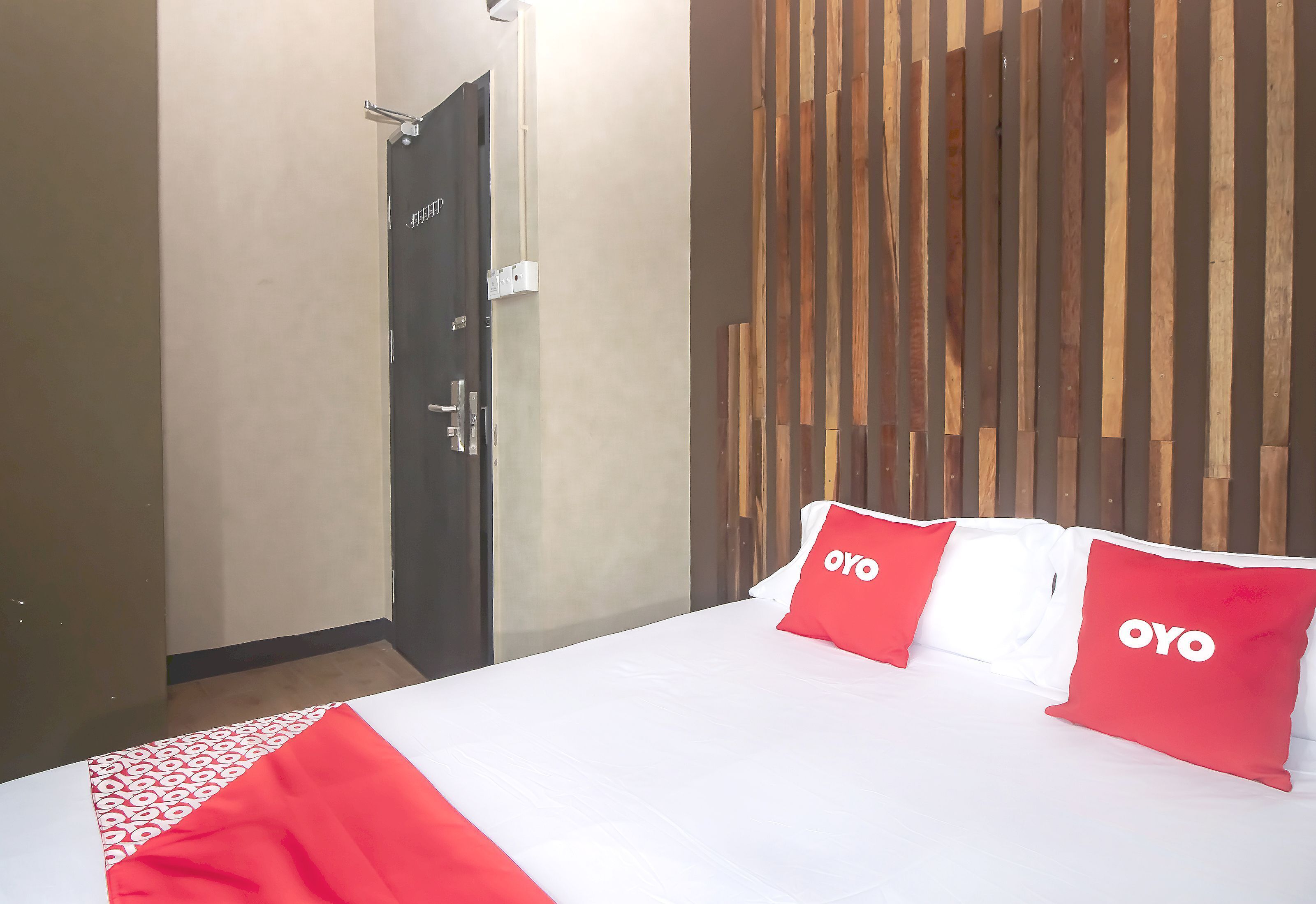 Quarto de hotel com uma cama, cabeceira de madeira e uma porta.