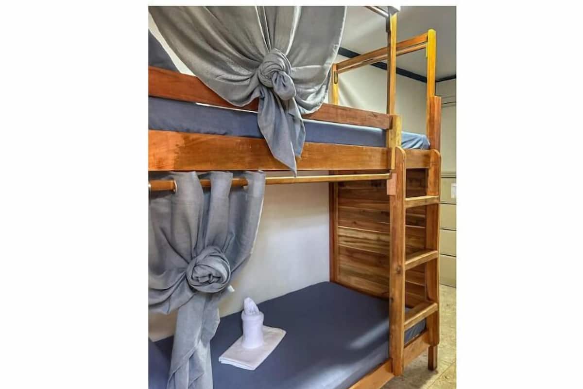 Uma cama beliche com estrutura de madeira e cortina cinza amarrada na cabeceira.