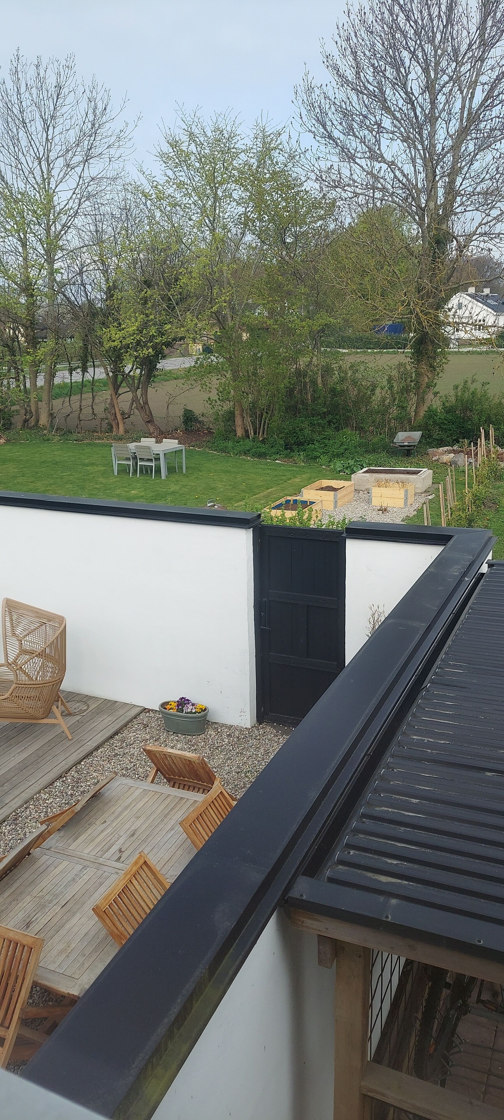 Um terraço no telhado com uma mesa pequena e cadeiras, um deck de madeira e uma área de jardim com árvores e gramado.