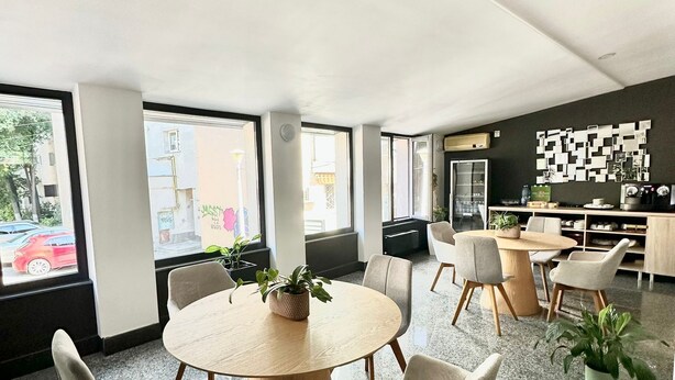 Um espaço de escritório moderno com uma mesa redonda de madeira, rodeada por cadeiras, grandes janelas e uma parede com padrão em preto e branco.
