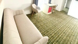 Quarto de hotel moderno com sofá, pequena mesa de escritório e área de refeições.