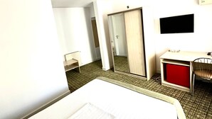 Quarto de hotel com uma cama grande, uma escrivaninha com cadeira, televisão e guarda-roupa.