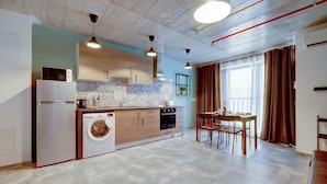 Cozinha moderna com máquina de lavar embutida, área de refeições com mesa e cadeiras, e uma janela grande com cortinas.