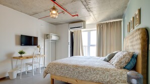 Quarto com uma cama, uma escrivaninha, uma cadeira e uma televisão.