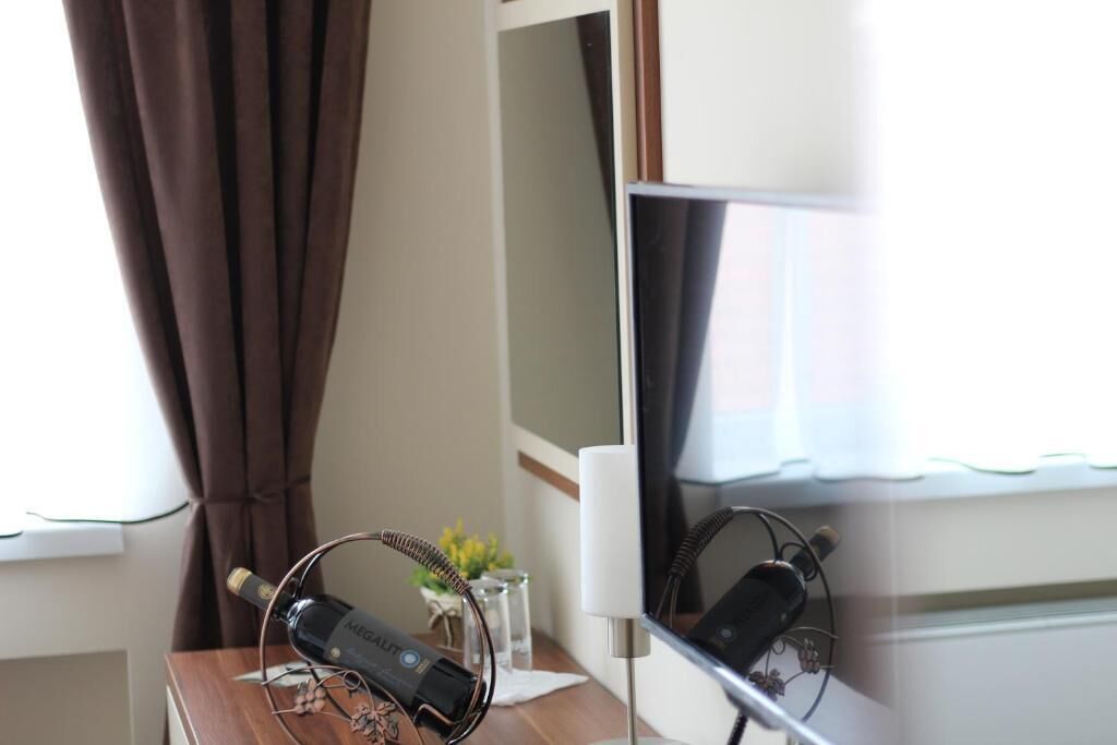 Quarto de hotel com uma escrivaninha de madeira, uma garrafa de vinho, um pequeno vaso com flores e uma televisão.