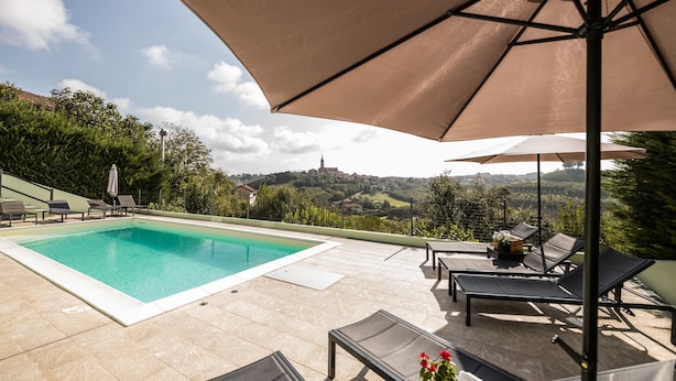 Piscina com espreguiçadeiras e guarda-sóis, cercada por um jardim bem cuidado e vista para colinas ao longe.