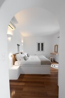 Quarto com cama embutida, paredes brancas, chão de madeira, uma mesinha e um espelho.