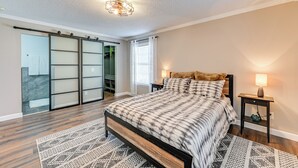 Quarto com cama, mesa de cabeceira, abajur, guarda-roupa com portas deslizantes e tapete estampado.