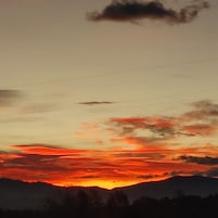 Um pôr do sol sobre uma paisagem montanhosa, com linhas de eletricidade em primeiro plano.
