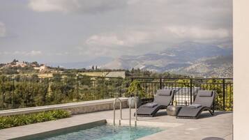 Uma área de piscina no terraço com duas espreguiçadeiras, uma mesa pequena com revista e bebidas, e vista da paisagem ao redor.