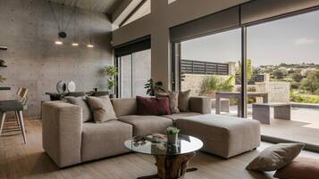 Uma sala de estar moderna com um amplo sofá modular, uma mesa de centro de vidro e vista para um jardim e colinas.