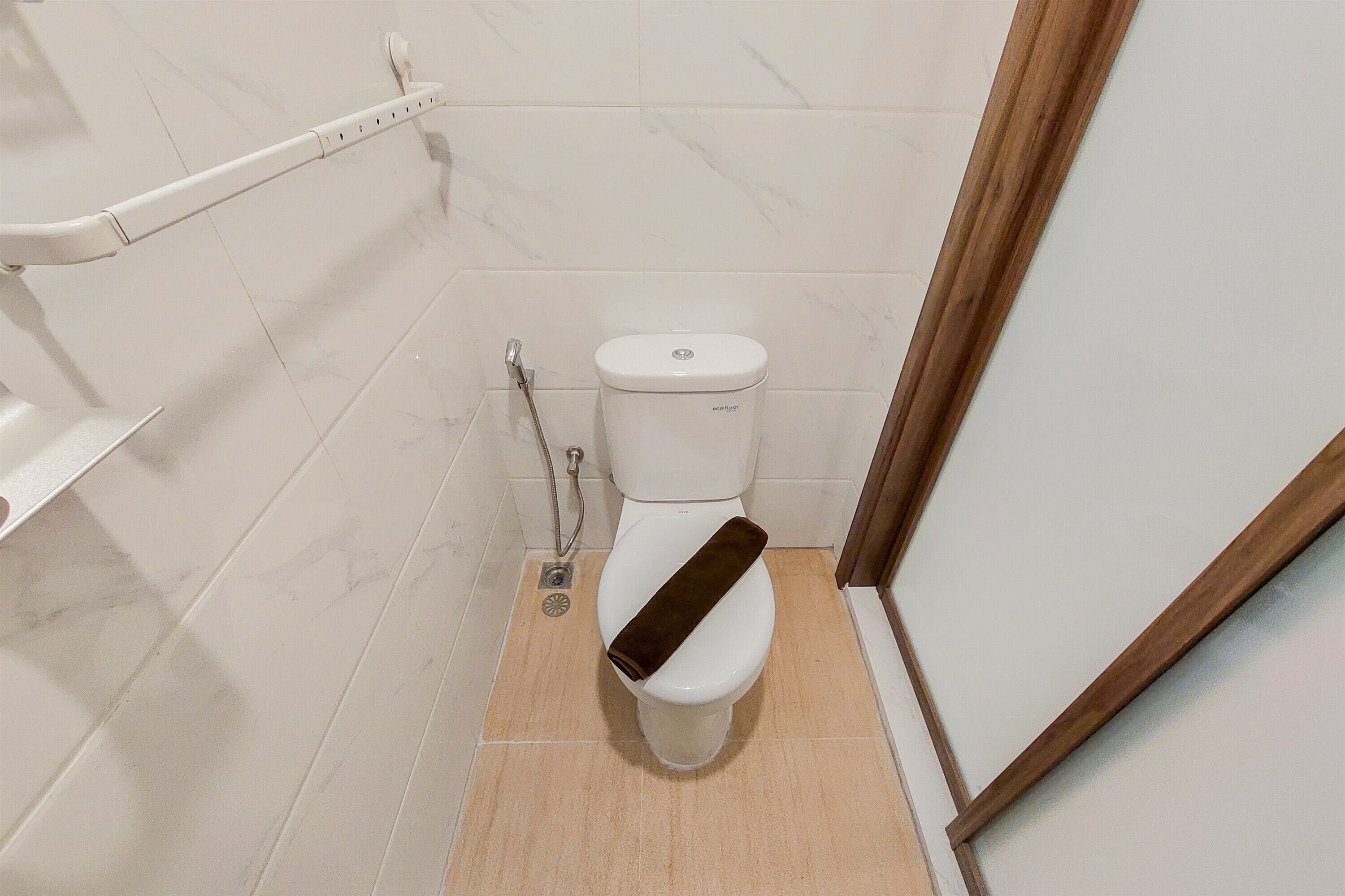 Um banheiro pequeno e moderno, com vaso sanitário branco, barra de apoio e área de chuveiro.