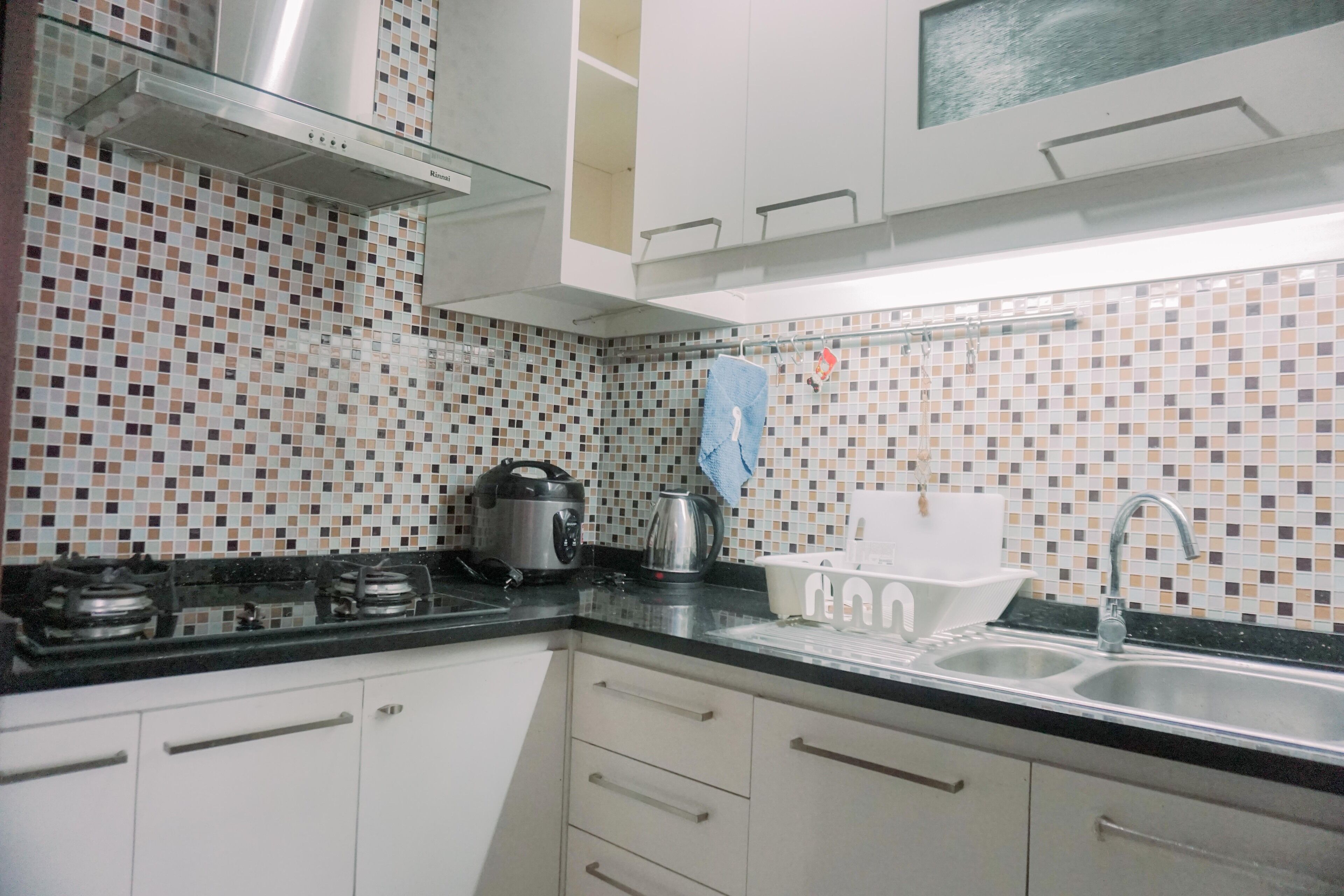 Cozinha com armários brancos, bancada preta e painel de azulejos.