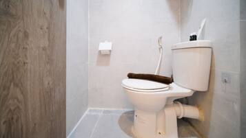 Casa de banho moderna com sanita branca, assento de madeira, suporte de papel higiénico branco e um cano à vista.
