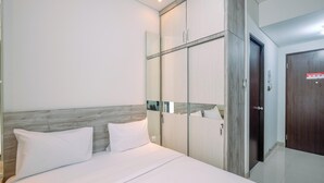 Quarto de hotel moderno com uma cama grande, cabeceira de madeira, guarda-roupa com espelho e uma porta com uma placa vermelha.