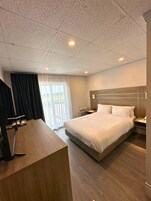 Quarto de hotel com uma cama grande, uma escrivaninha e vista para o exterior através de uma janela com cortinas.