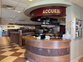 Uma área de recepção com um balcão curvo, uma placa com a palavra 'ACCUEIL' e um balcão de check-in ao fundo.