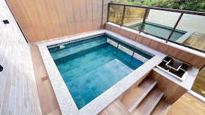Piscina retangular com borda revestida de azulejos, deck de madeira e guarda-corpo de vidro.