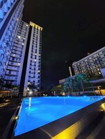 Vista noturna de um hotel com piscina, edifícios altos e palmeiras.