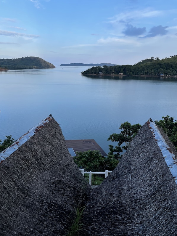 Vista de um lago tranquilo com uma construção de colmo em primeiro plano e colinas ao longe.
