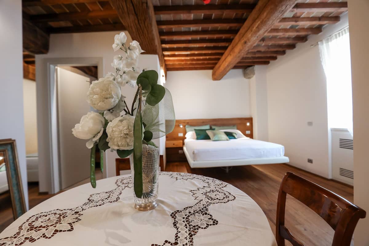 Um quarto com uma cama, uma mesa com toalha rendada e um vaso com flores.