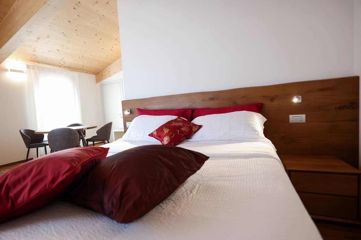 Quarto com cabeceira de madeira, roupa de cama branca e almofadas vermelhas e bordô.