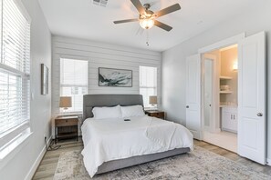 Quarto com cama, mesas de cabeceira, ventoinha no teto e vista para um cômodo adjacente.