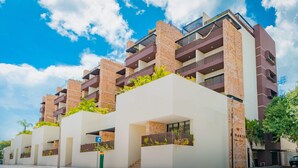 Um edifício moderno de vários andares com varandas, área de estacionamento e céu azul.
