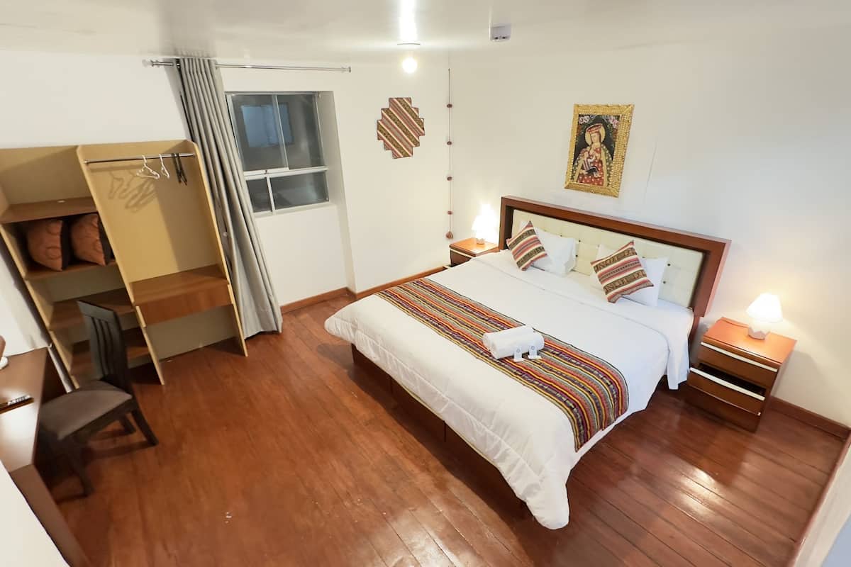 Quarto com cama, escrivaninha de madeira, cadeira, guarda-roupa e janela com cortinas.