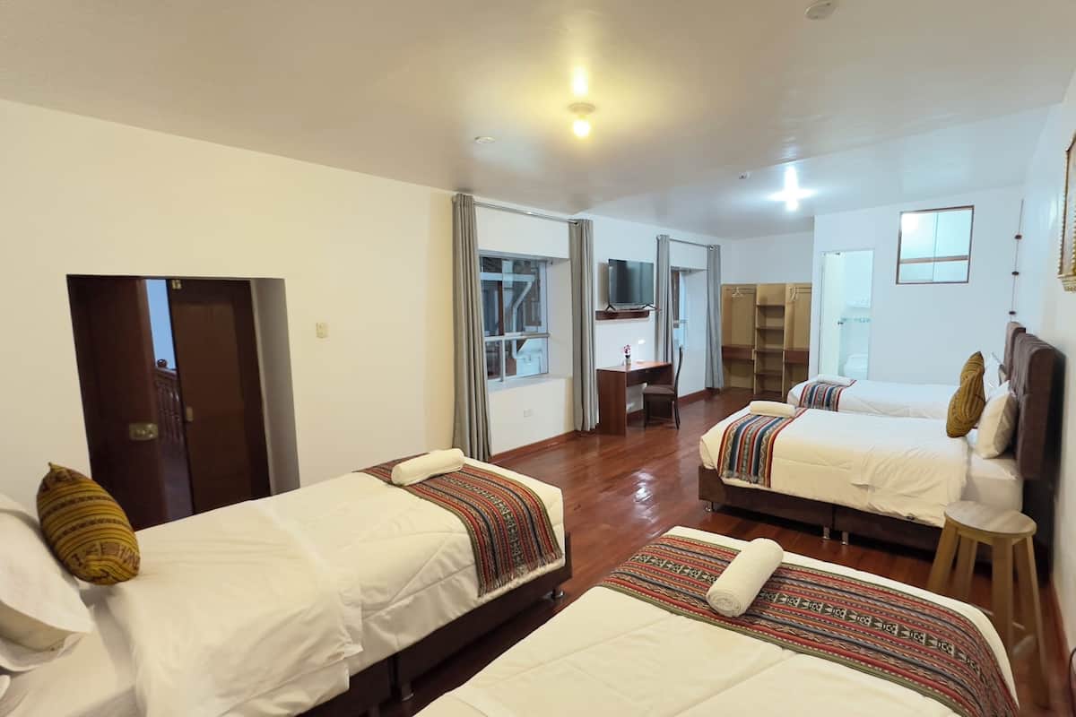 Quarto de hotel com duas camas, uma escrivaninha, televisão e banheiro visível por uma porta aberta.