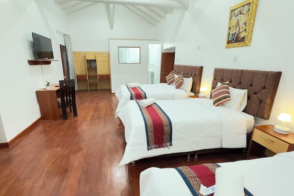 Quarto de hotel com duas camas, televisão, secretária e banheiro visível através de uma porta aberta.