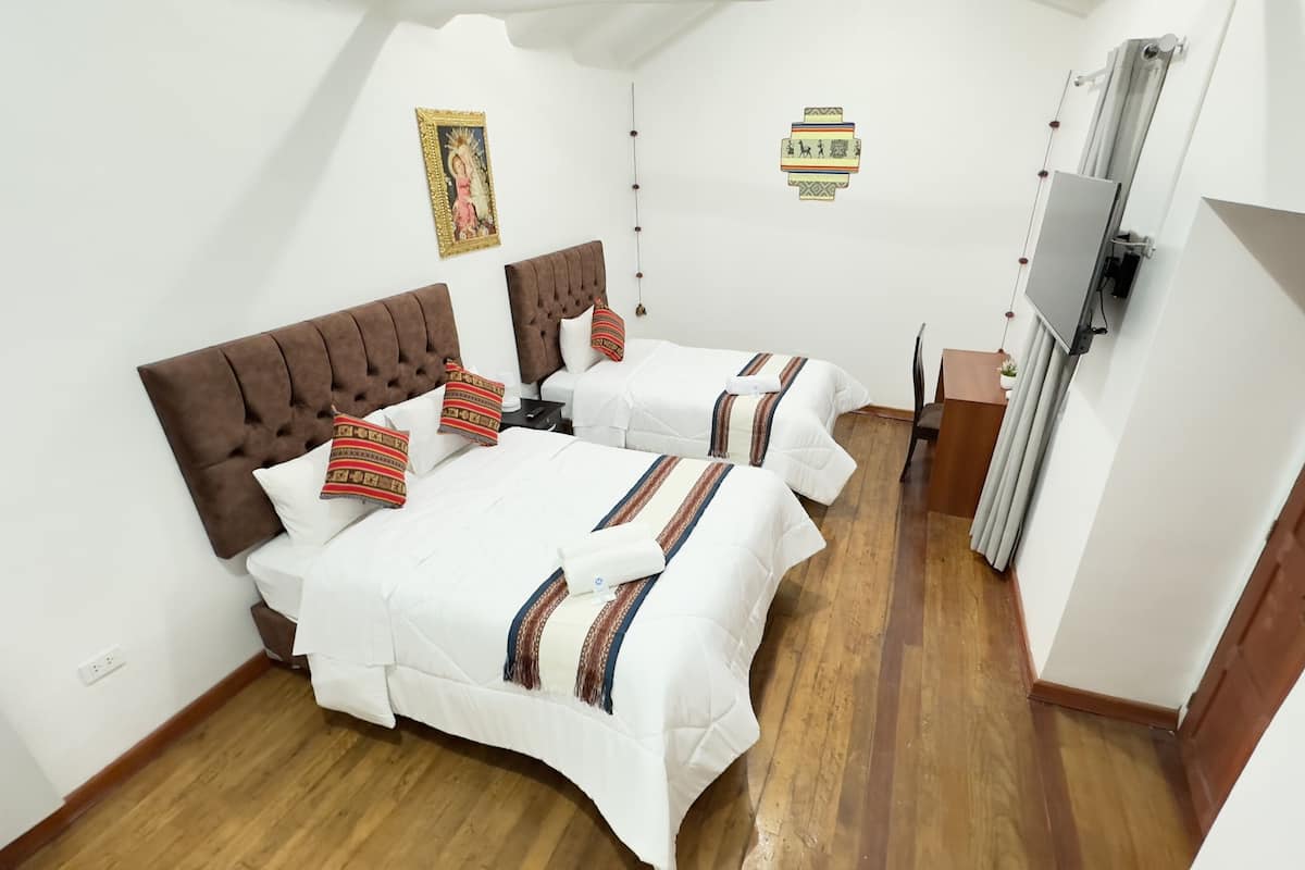 Quarto com duas camas, piso de madeira, cabeceira marrom e uma pequena mesa com cadeira.