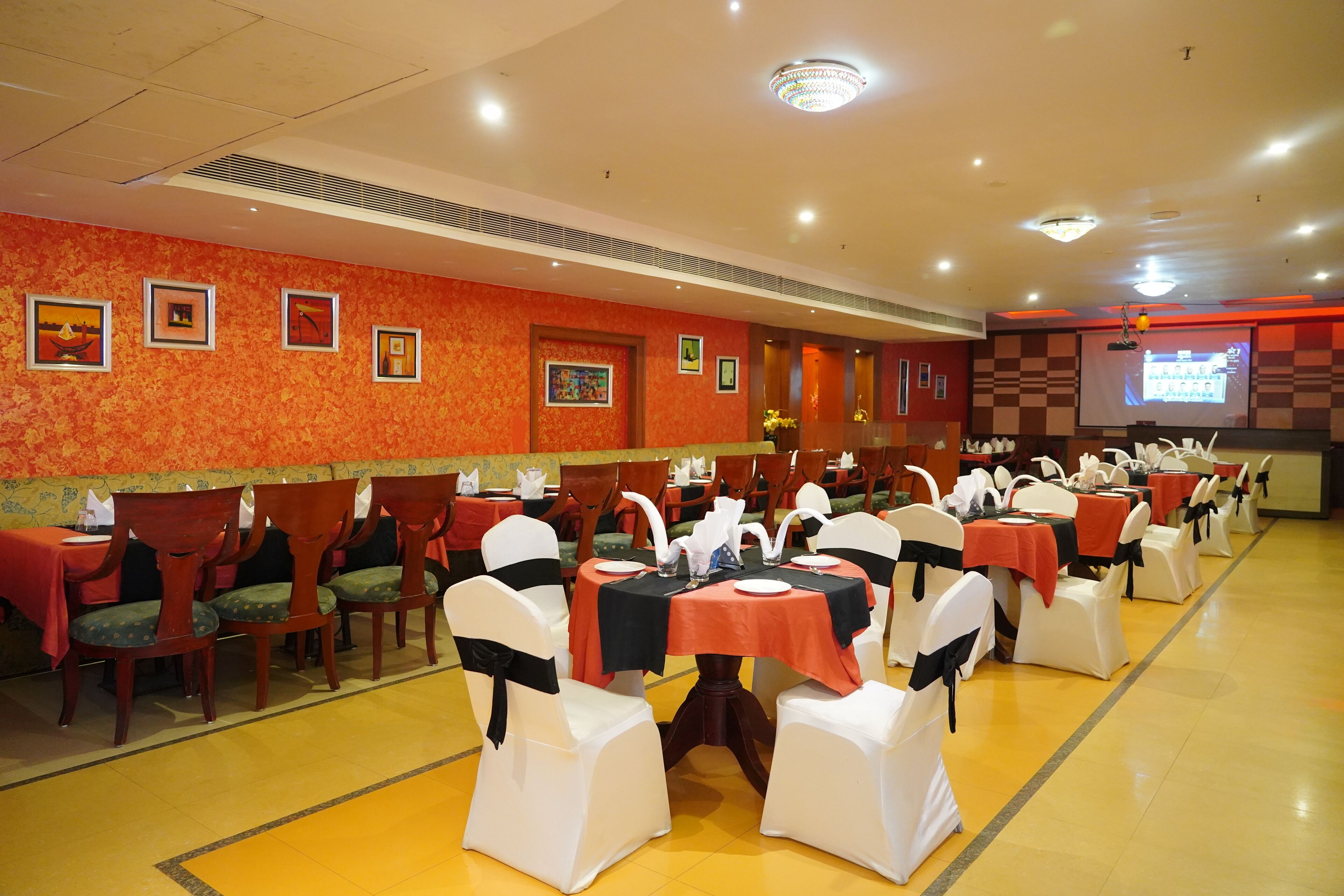 Uma sala de banquetes com mesas e cadeiras organizadas em fileiras e uma tela de projeção.