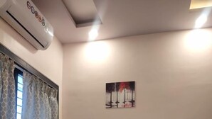 Quarto de hotel com uma cama, janela com cortinas estampadas, ar condicionado e um quadro na parede.