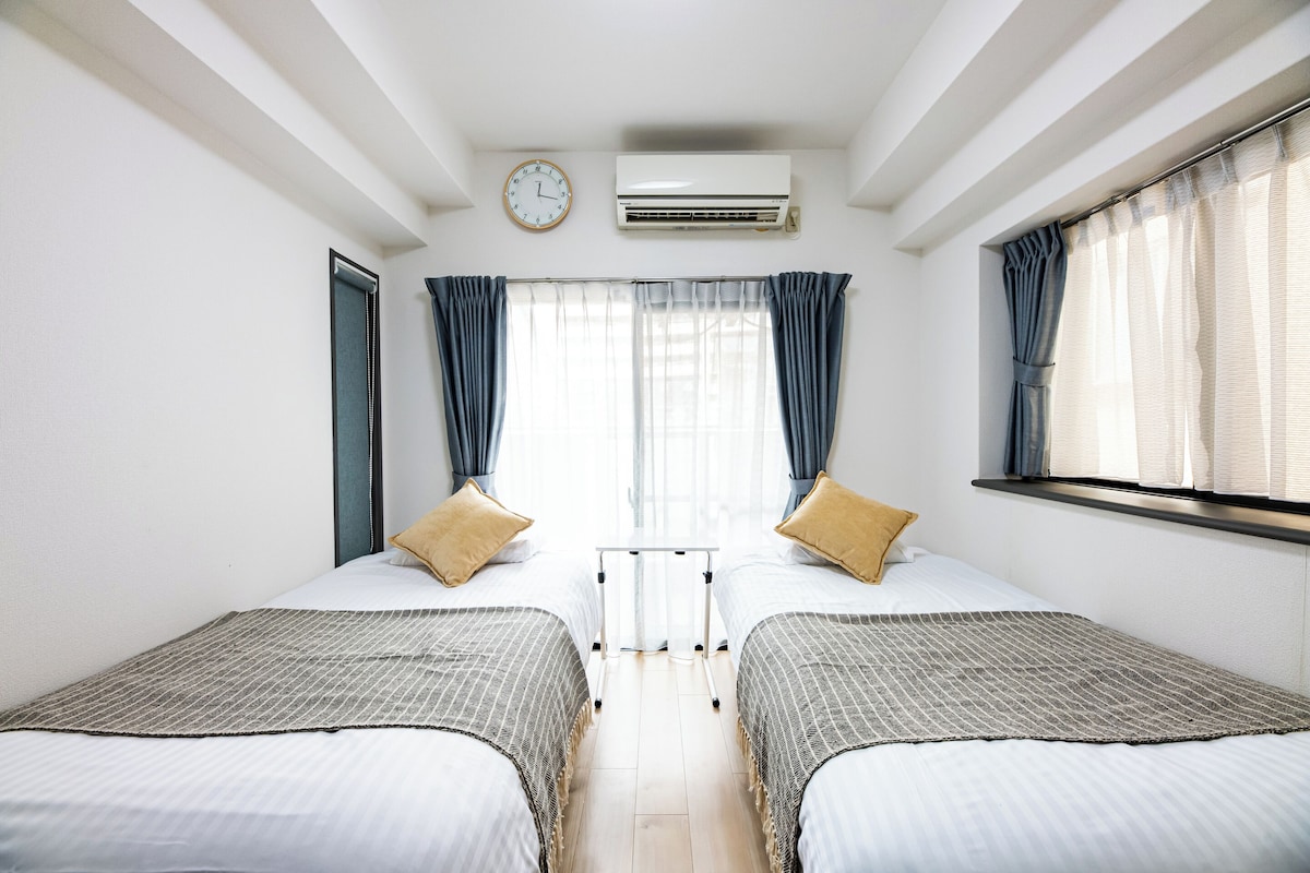 Quarto de hotel com duas camas, um relógio, ar condicionado e uma janela com cortinas.