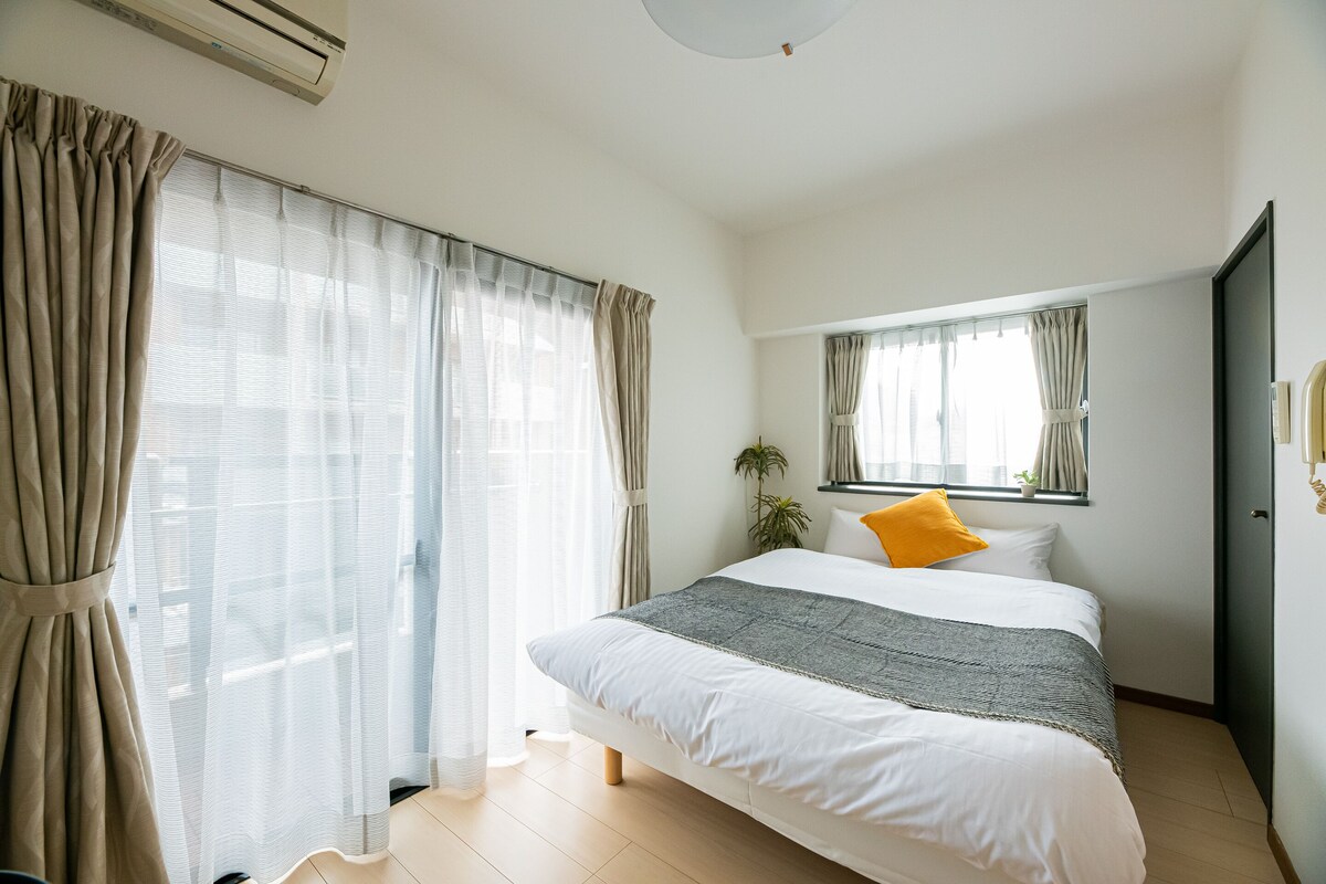 Um quarto com cama, cortinas, uma janela e uma planta.