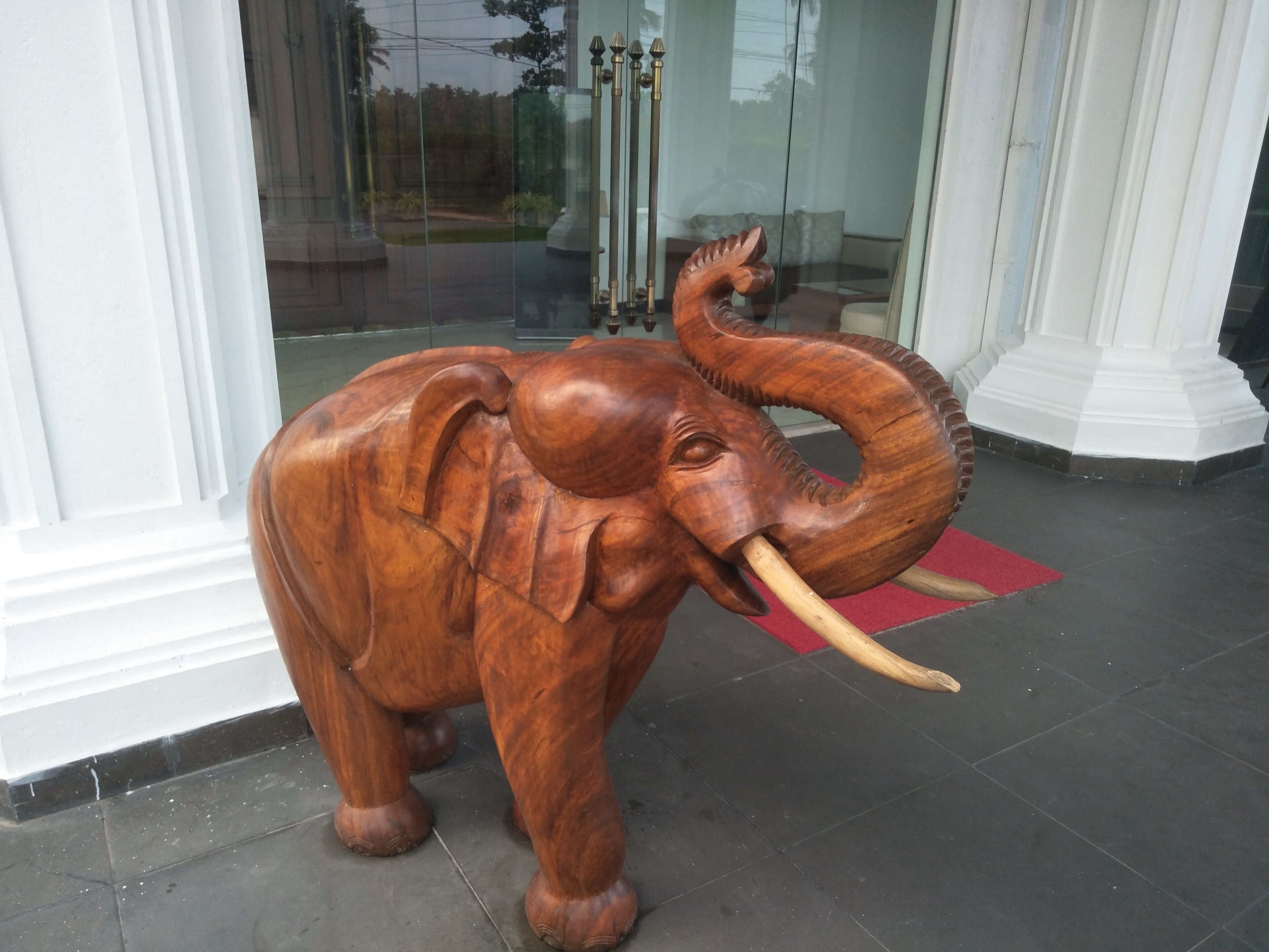 Uma estátua de elefante de madeira em frente a um edifício com colunas brancas e um tapete vermelho.