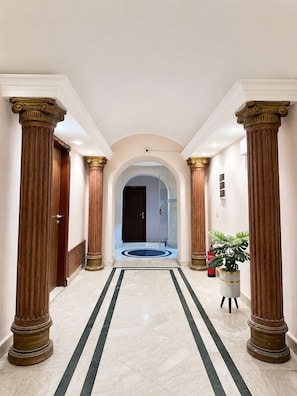 Um corredor com piso de mármore, colunas e uma porta no final.