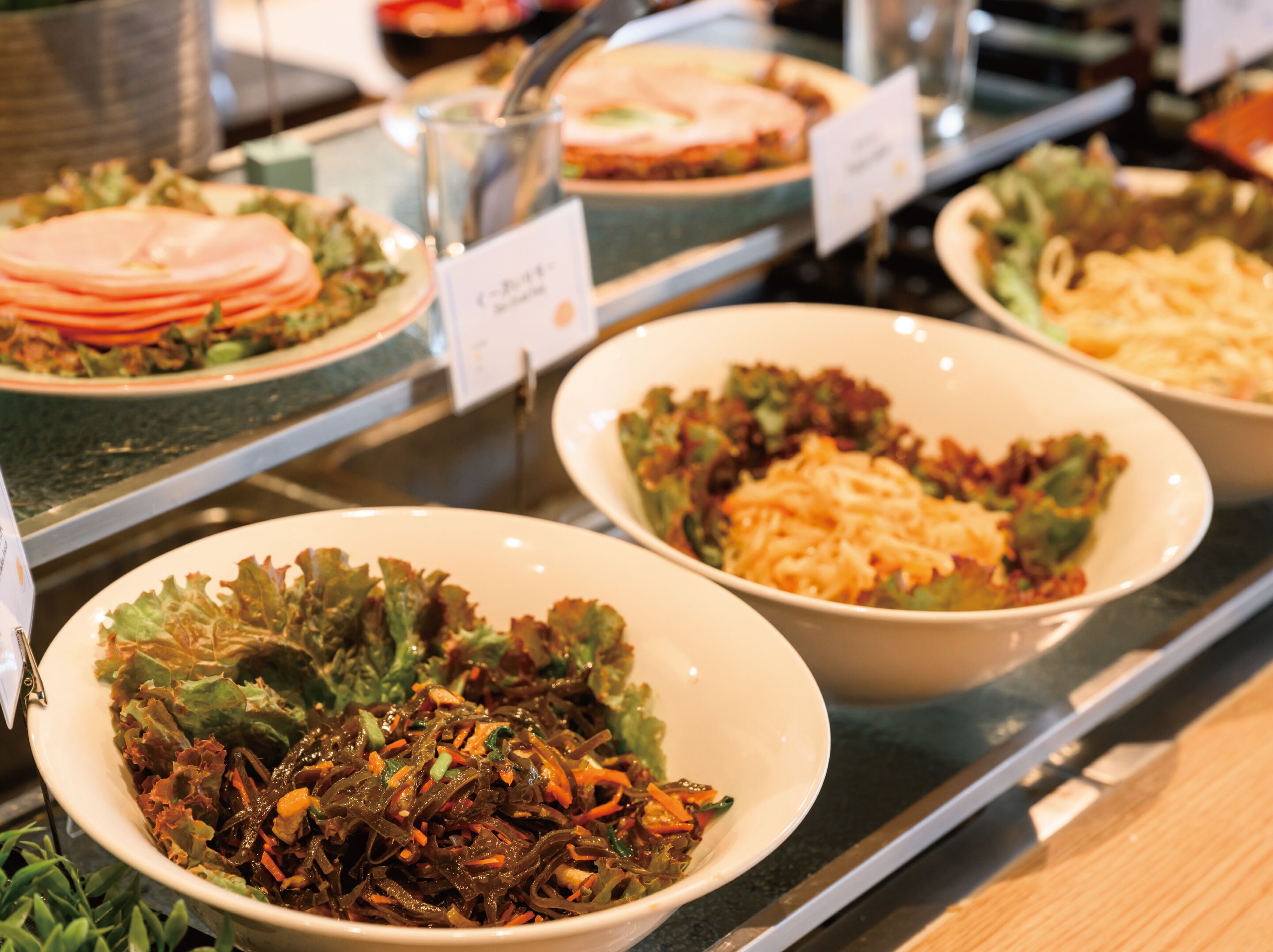 Buffet com diversos pratos, incluindo saladas, massas e outros alimentos já preparados.