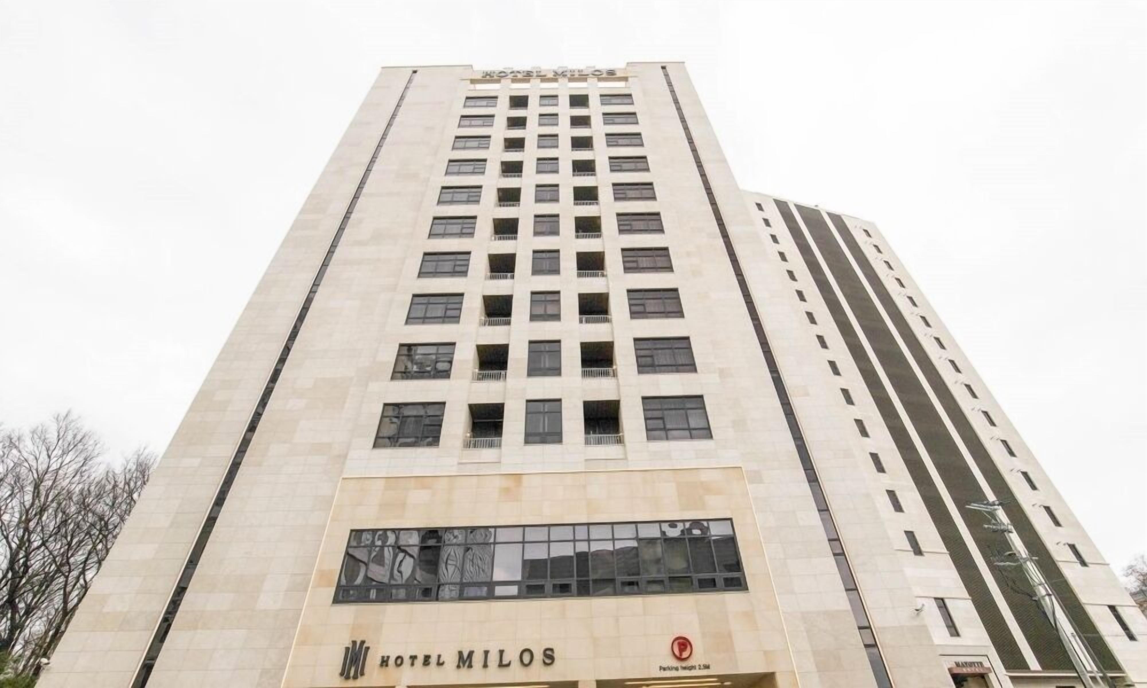 Um prédio alto de hotel com a placa "Hotel Milos" na fachada.