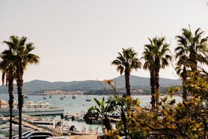 Marina com barcos atracados, palmeiras e paisagem montanhosa ao fundo.