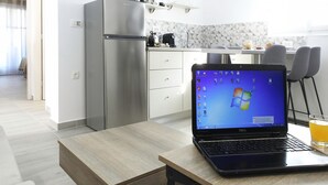 Uma cozinha moderna com geladeira de aço inoxidável, um laptop sobre uma mesa de madeira, e uma mesa de café da manhã com um copo de suco de laranja.