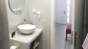 Casa de banho com lavatório branco, espelho, secador de cabelo e toalheiro.