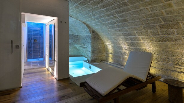 Um quarto de spa com parede de pedra, piso de madeira, banheira e espreguiçadeira.